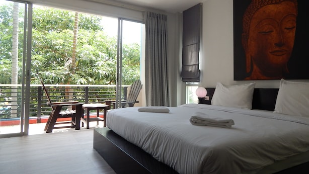Quarto moderno com uma cama grande, vista para o verde pela varanda e uma estátua de Buda na parede.