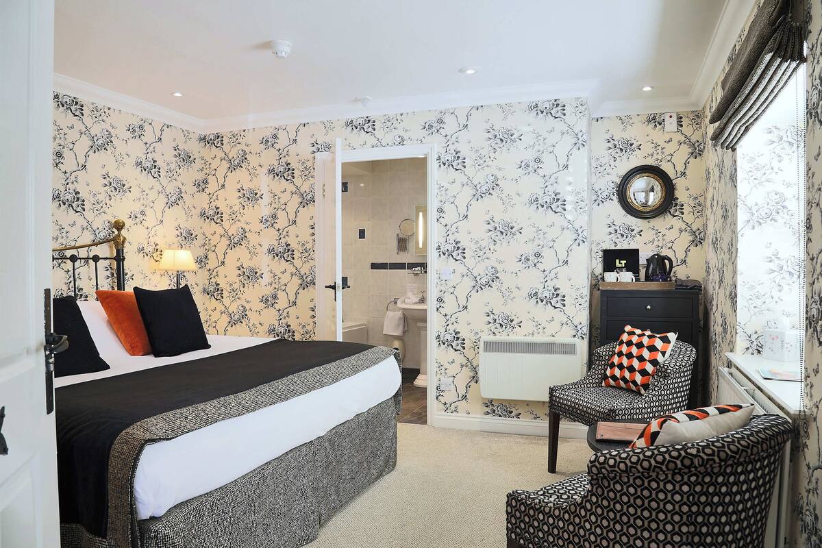Quarto de hotel com uma cama grande, uma cadeira, uma cômoda e vista para o banheiro.