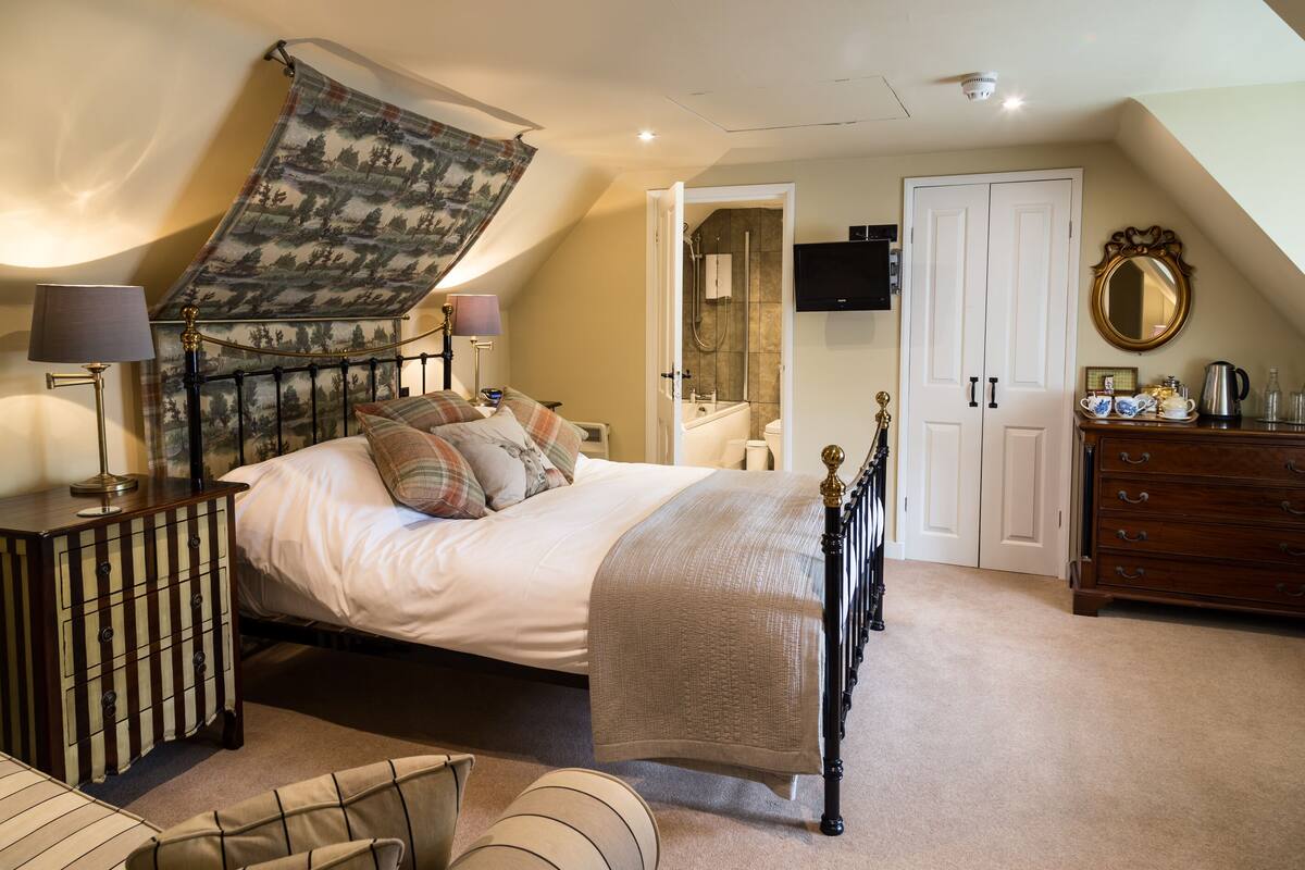 Quarto com cama, mesas de cabeceira, cômoda, espelho e porta para um banheiro.