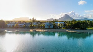 Resort com villas na praia, piscina e montanhas ao fundo.