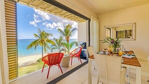 Uma varanda com vista para a praia e oceano, uma mesa de jantar com cadeiras e um vaso com planta.