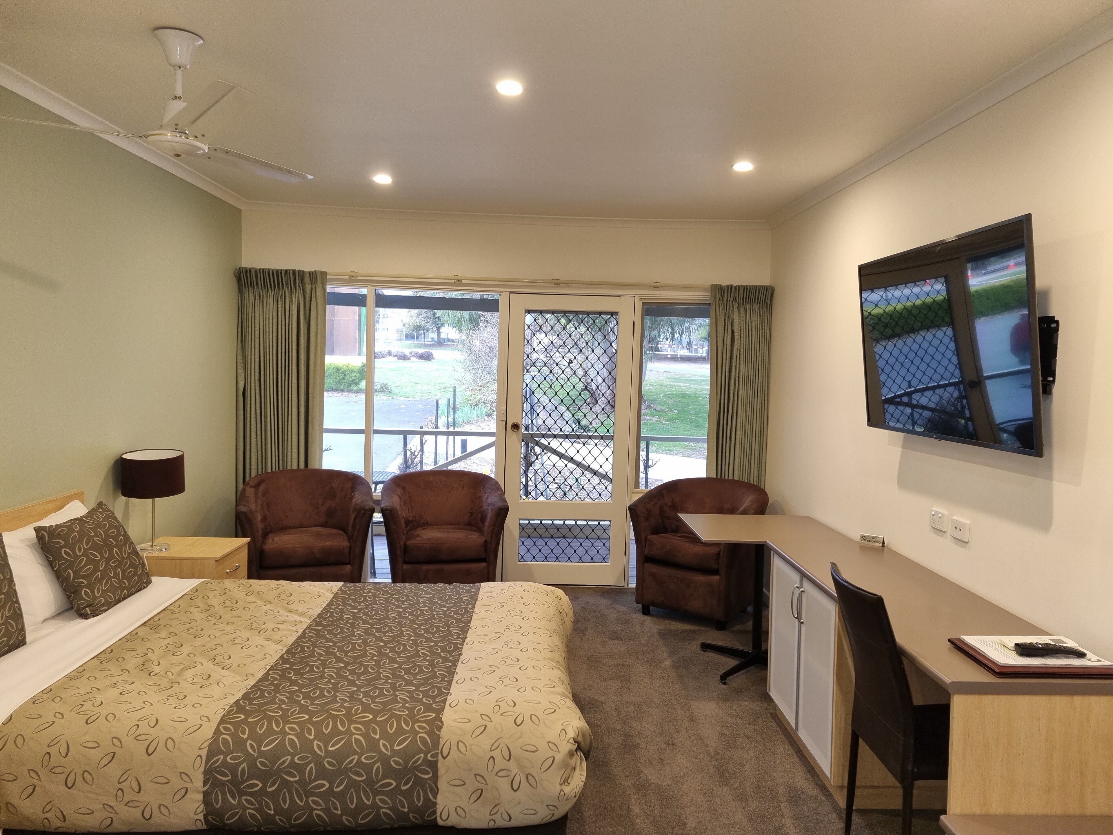 Quarto de hotel com cama, duas cadeiras, escrivaninha, televisão e varanda com vista.