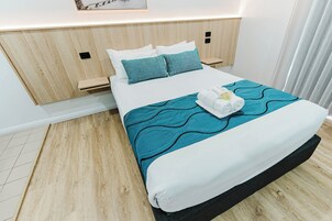 Uma cama bem arrumada com um edredom verde-água e branco, um travesseiro branco e uma toalha dobrada na cama.