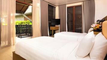 Quarto de hotel com uma cama grande, televisão e varanda com vista para vegetação.