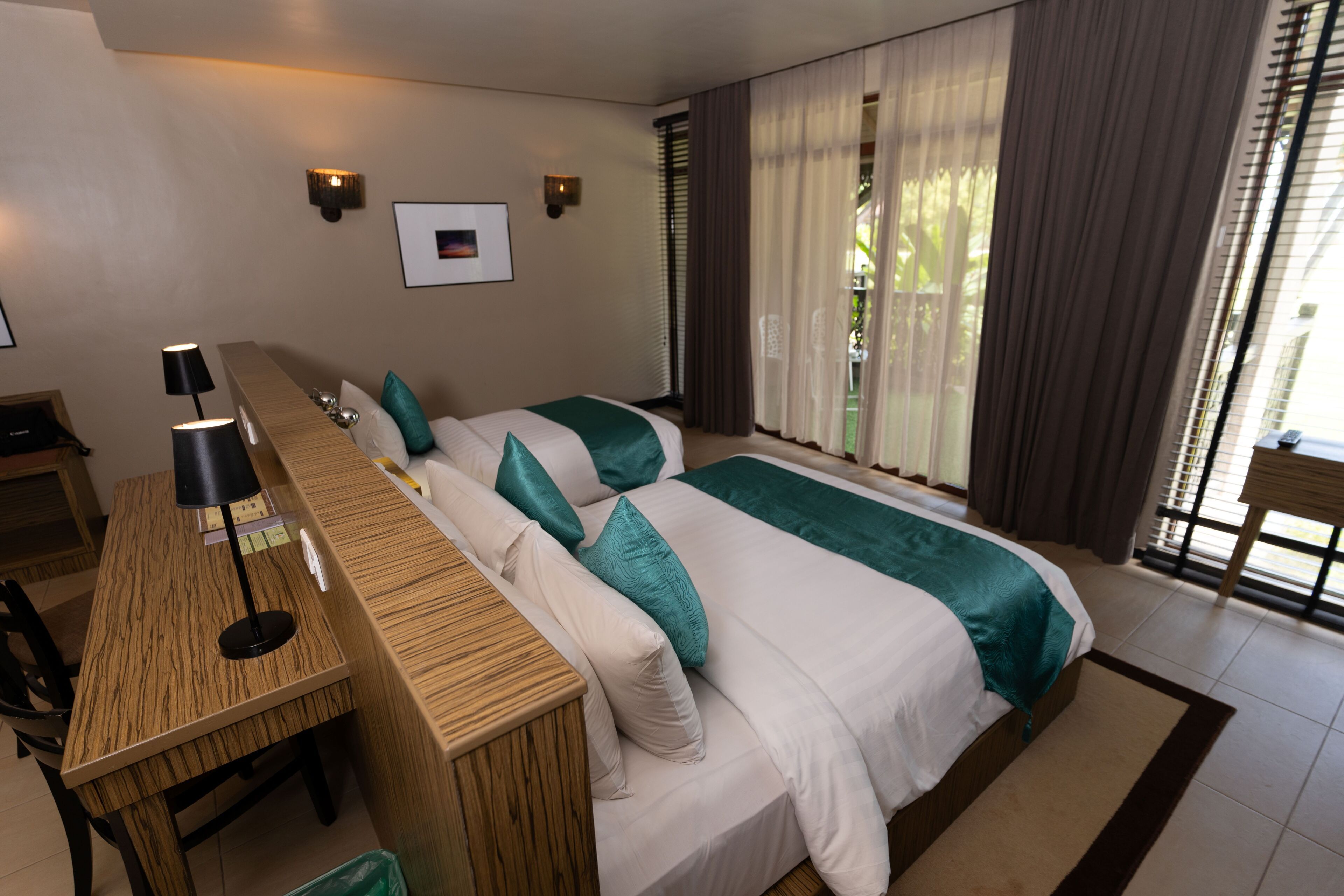 Quarto de hotel com cama, escrivaninha e janela com cortinas.
