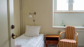 Um quarto com uma cama, mesa de cabeceira, cadeira, janela e radiador.