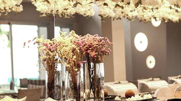 Interior de restaurante com vários vasos de flores no balcão, espaço para buffet e design moderno.