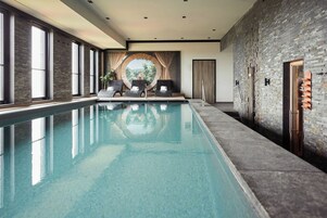 Piscina interior com parede de pedra e grandes janelas.