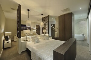 Quarto moderno com uma cama grande, mesas de cabeceira, um criado-mudo, escrivaninha, espelho e um banco embutido.