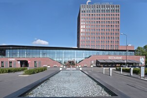 Um edifício moderno com um cassino e restaurante no andar térreo, uma fonte no centro e um prédio alto ao fundo.