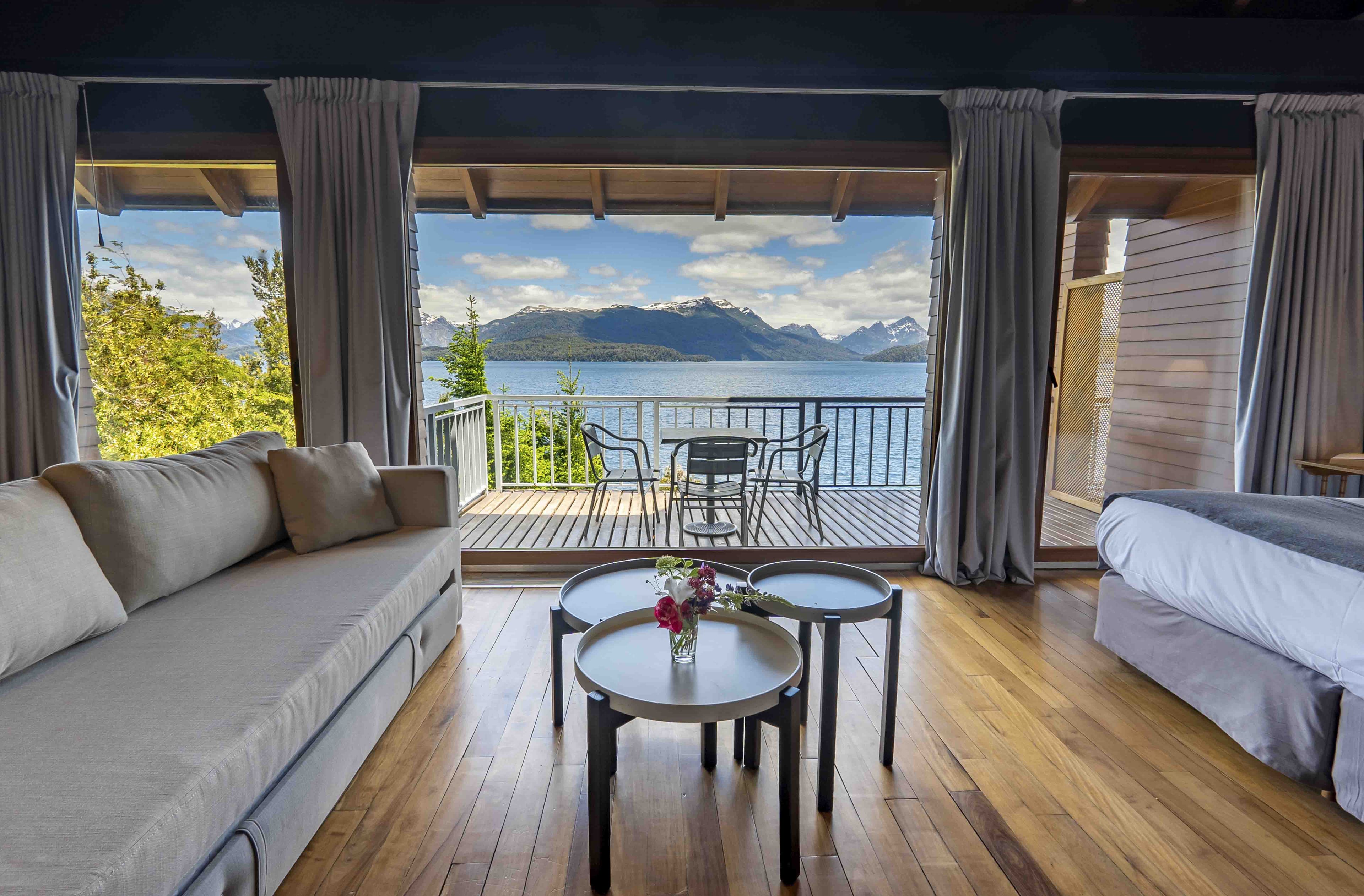 Quarto com deck de madeira, sofá, cama e mesa com um vaso de flores.