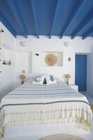 Quarto com cama, duas mesas de cabeceira, porta azul e luminária fixada na parede.