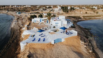 Um resort costeiro com edifícios brancos, uma praia arenosa e área de piscina.