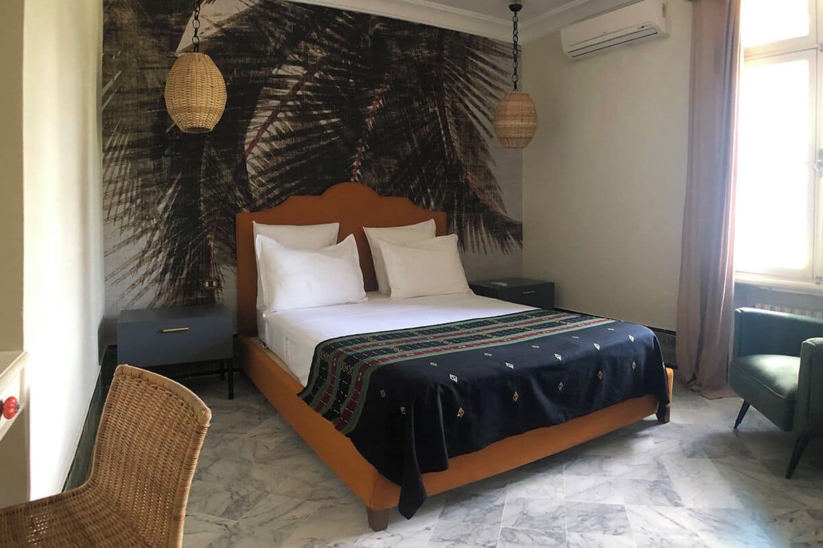 Quarto com cama, mesas de cabeceira, uma cadeira e uma janela.