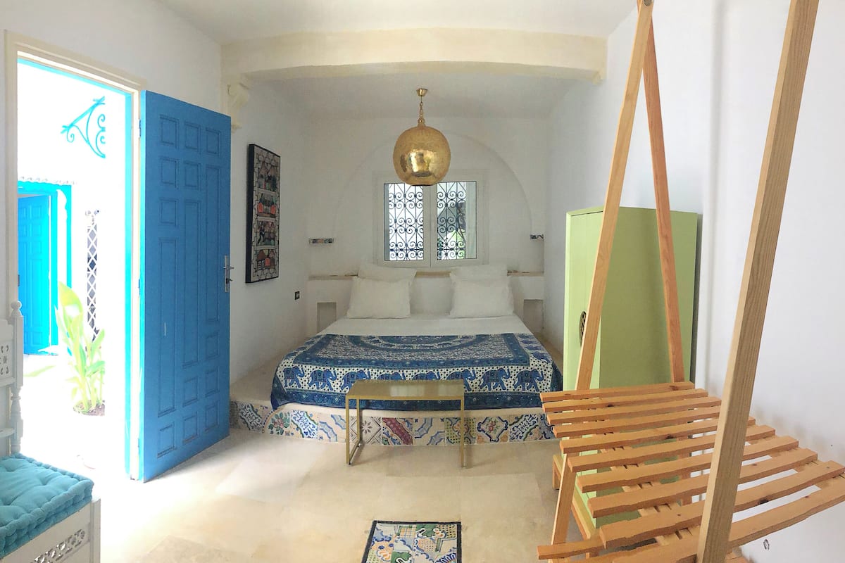 Quarto com cama, cadeira suspensa, janela e porta.