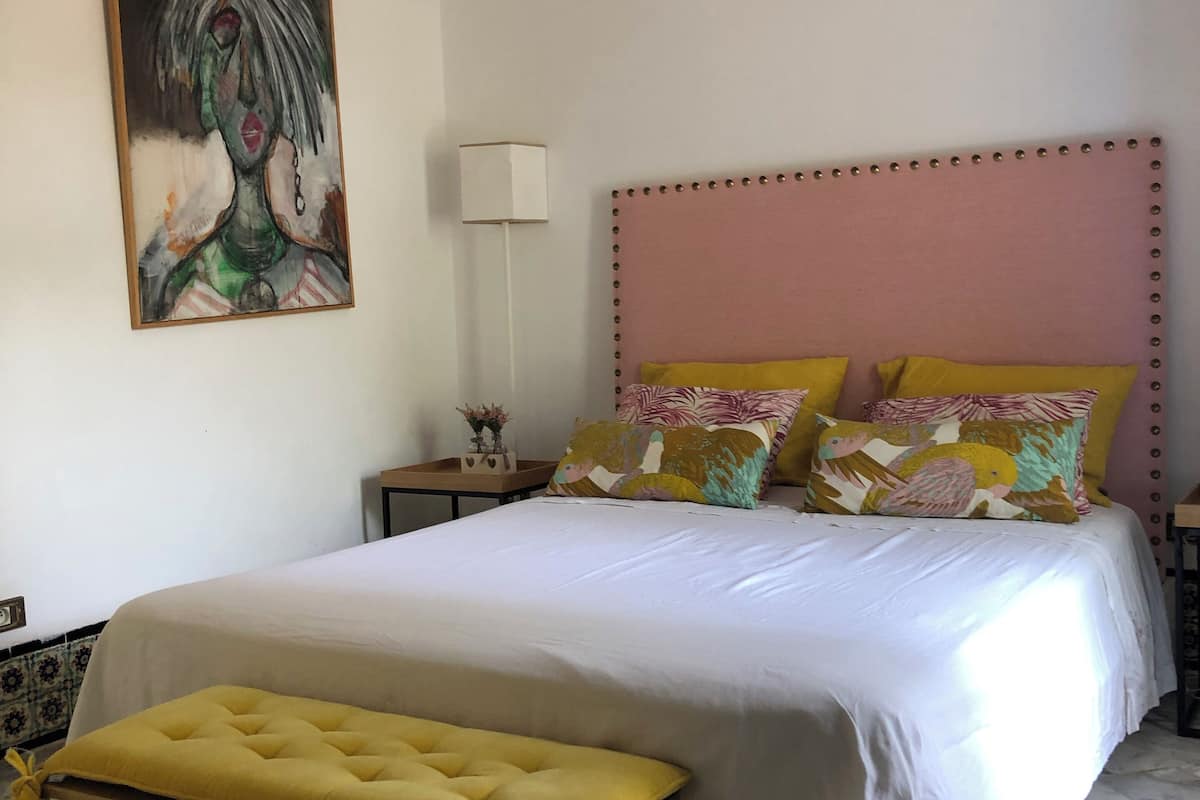 Um quarto com uma cama grande, uma mesinha de cabeceira, um abajur e um quadro na parede.