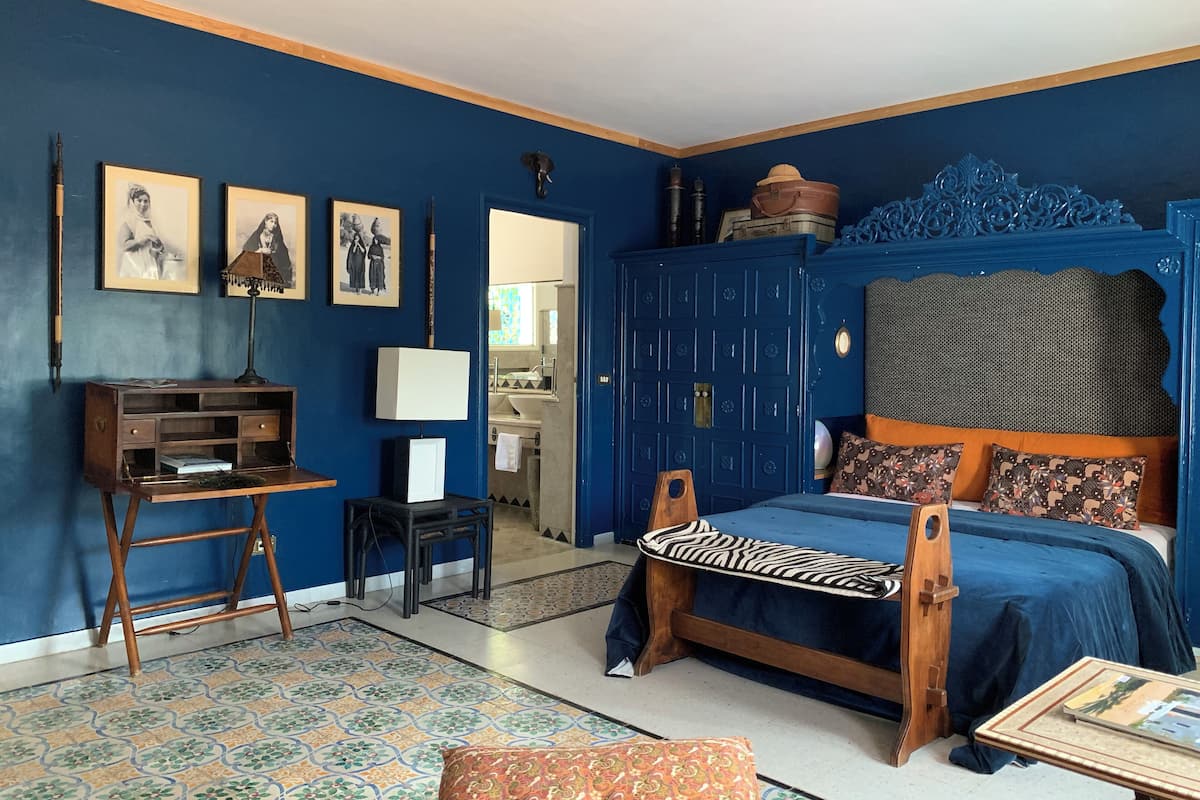 Um quarto com cama, mesa de cabeceira de madeira, escrivaninha e guarda-roupa.