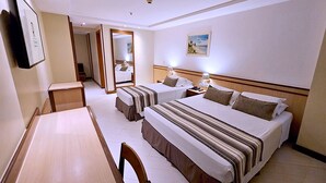 Quarto de hotel com duas camas, uma escrivaninha, uma cadeira, um espelho e um quadro na parede.