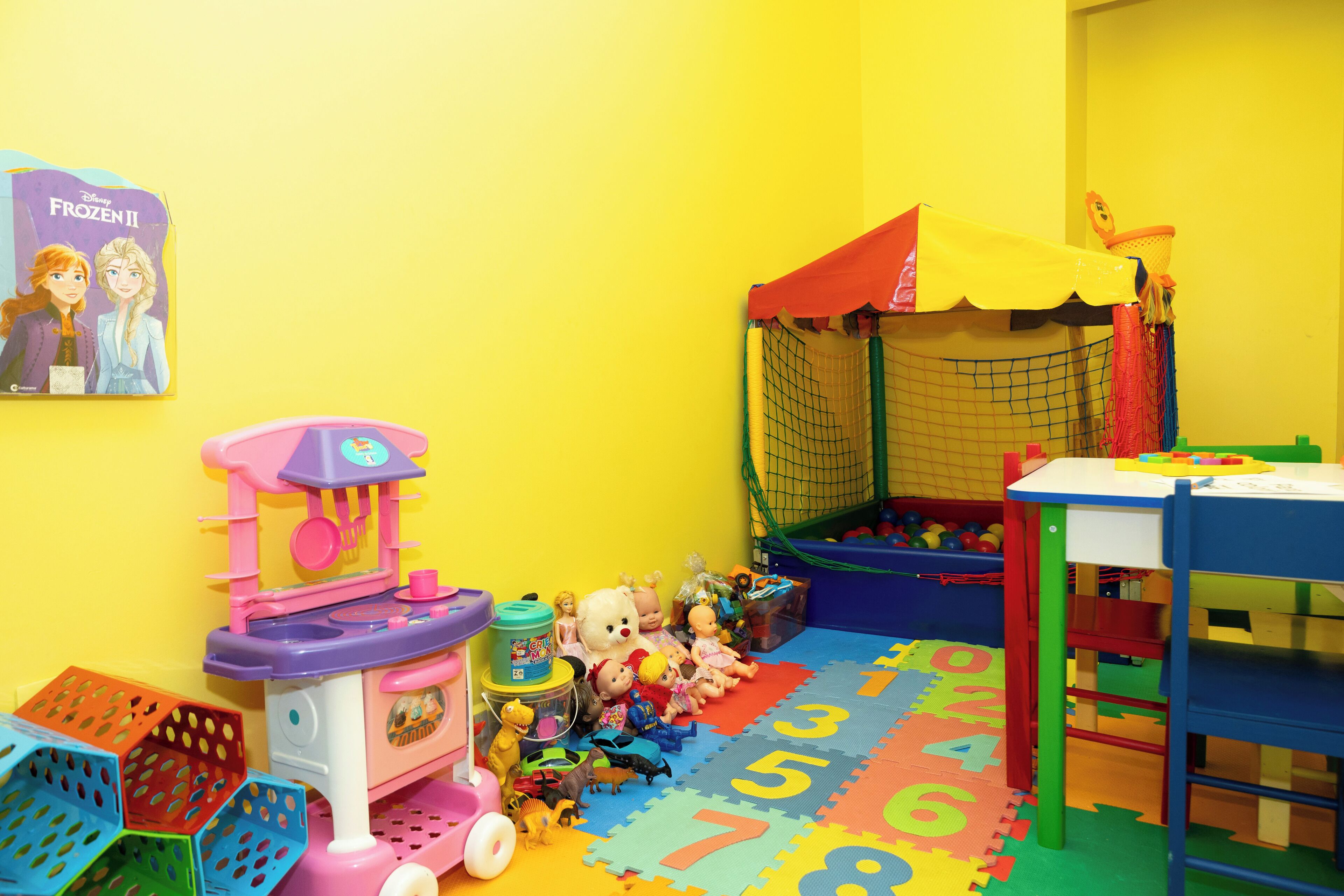 Uma sala de jogos infantil com casinha, piscina de bolinhas e diversos brinquedos.
