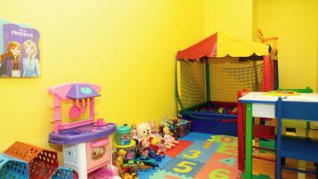 Uma sala de jogos infantil com casinha, piscina de bolinhas e diversos brinquedos.