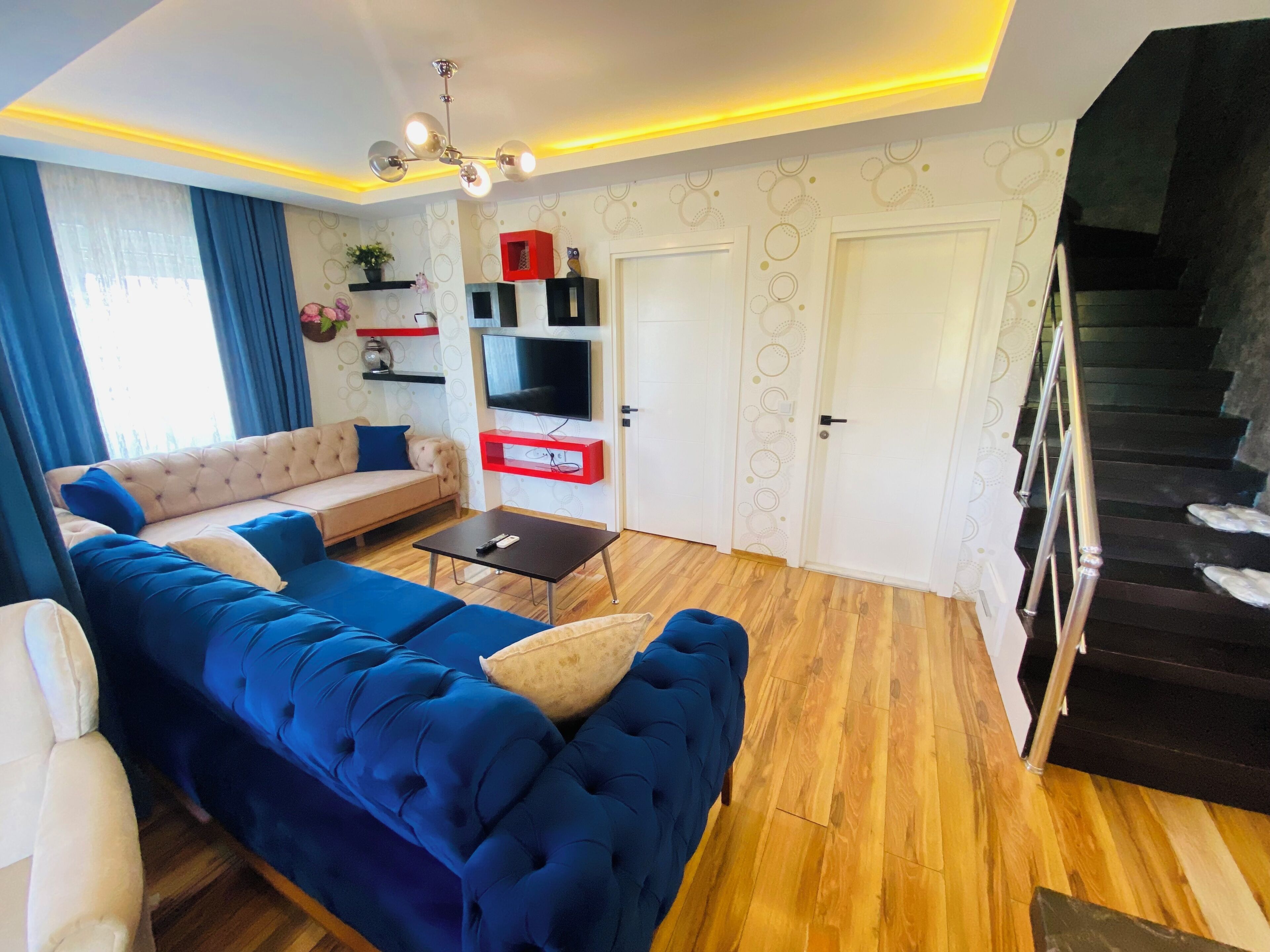 Uma sala de estar com um sofá azul, uma televisão, uma mesa de centro e uma escada.