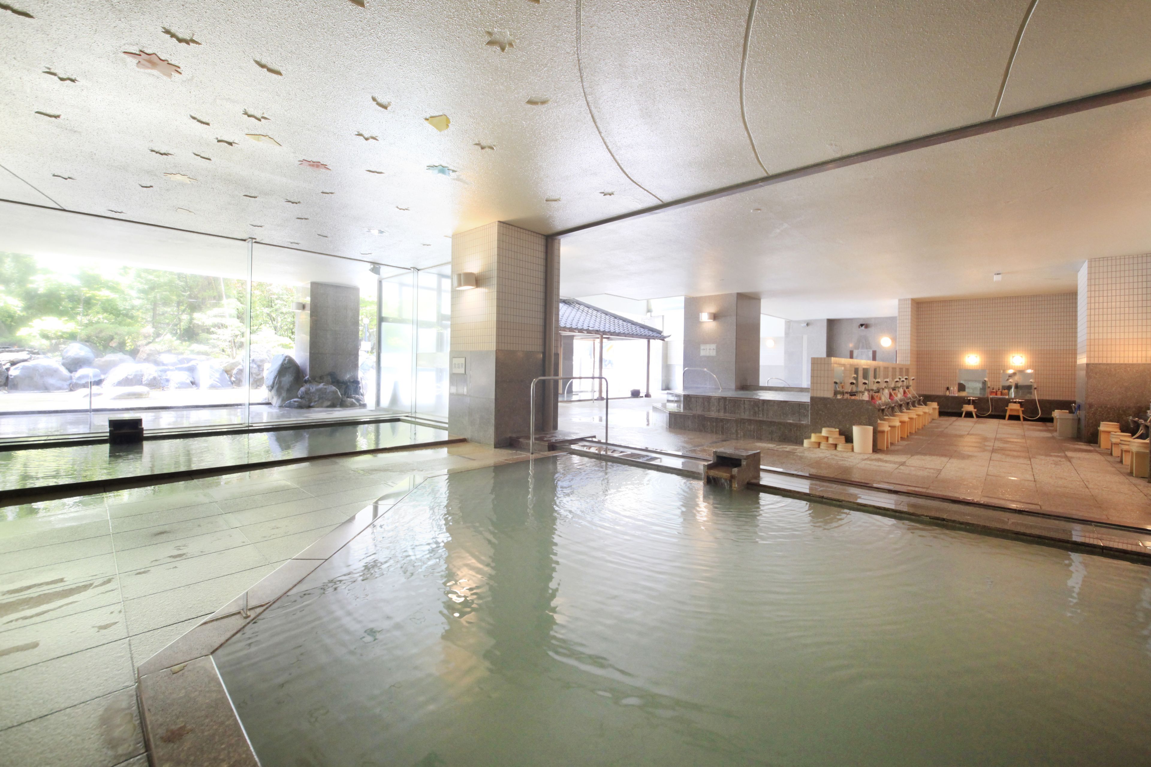Uma grande piscina interior com paredes de vidro transparente, chão ladrilhado e área de estar com bancos.