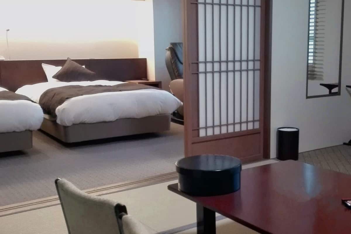 Quarto de hotel com duas camas, uma secretária de madeira, uma cadeira e vista para o mar.