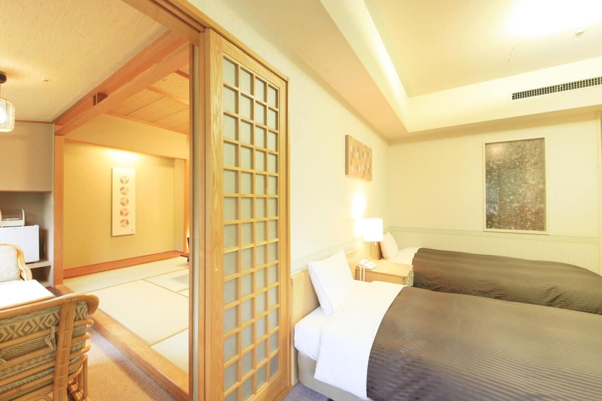 Quarto de hotel com cama, cadeira, escrivaninha, espelho e porta deslizante.