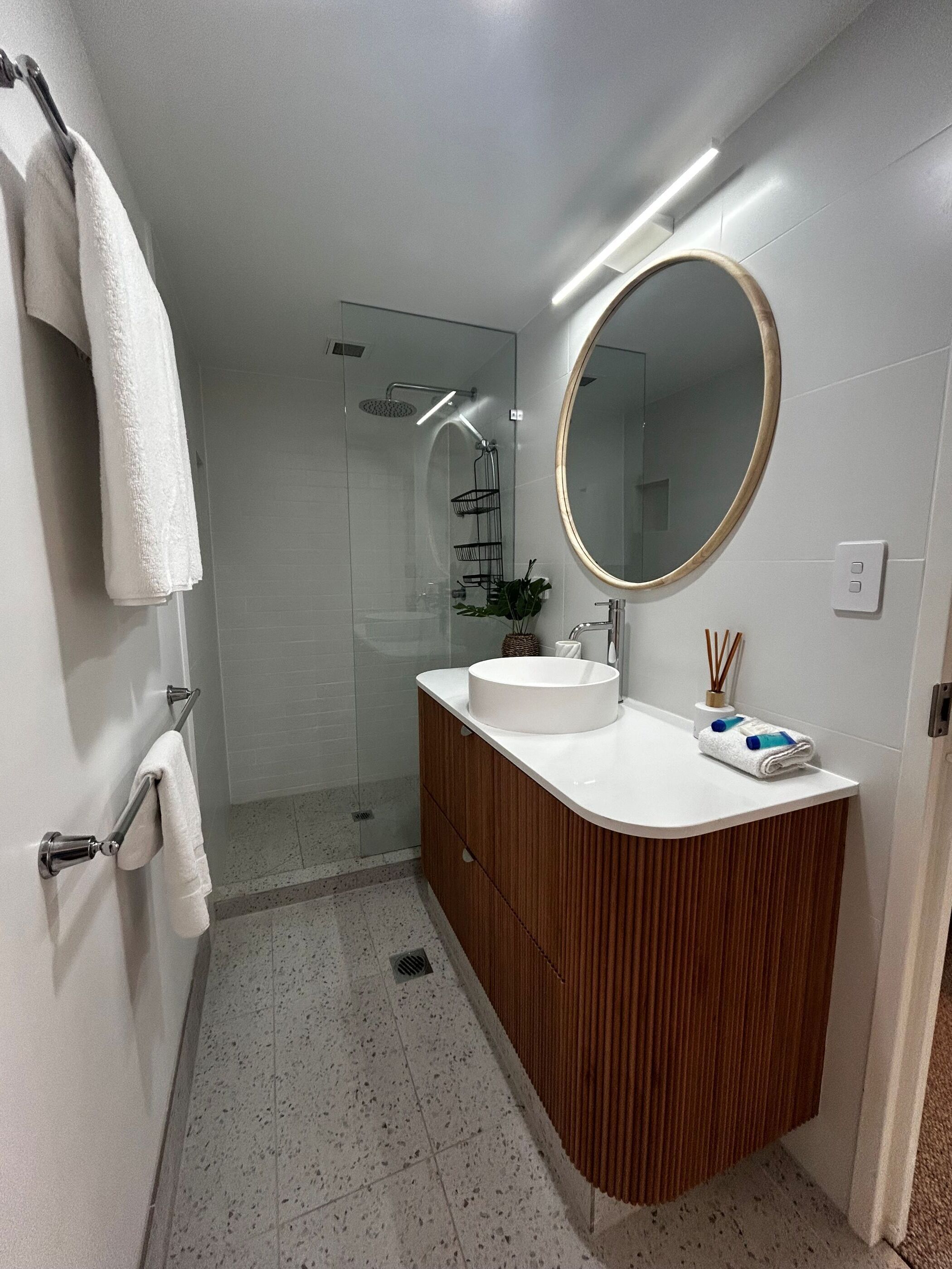 Uma casa de banho moderna com uma toucador branco, um espelho redondo e uma cabine de duche com vidro.