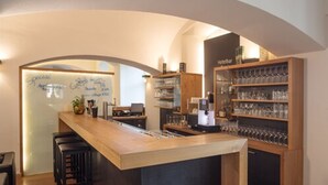Uma área de bar com balcão de madeira, banquetas, uma vitrine de vidro e uma placa com a inscrição 'Hotelbar'.