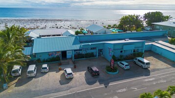 Hotel na praia com estacionamento, vários carros e vista para o mar.