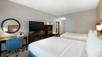 Quarto de hotel com cama, escrivaninha com cadeira, televisão, espelho e mesa de cabeceira.