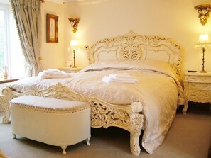 Quarto clássico e ornamentado, com uma cama grande, mesas de cabeceira harmoniosas e um abajur decorativo.