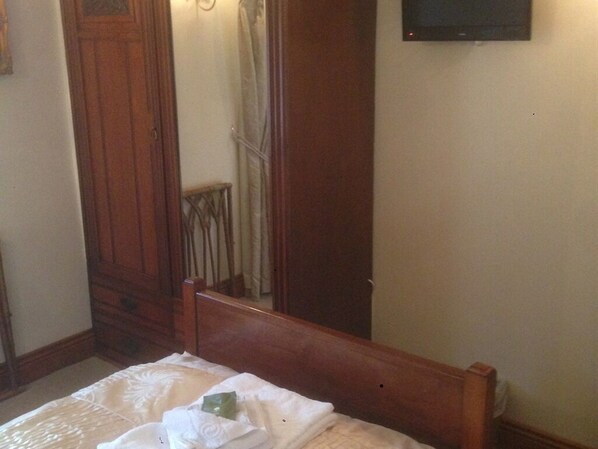 Quarto com cama de madeira, um espelho e televisão na parede.
