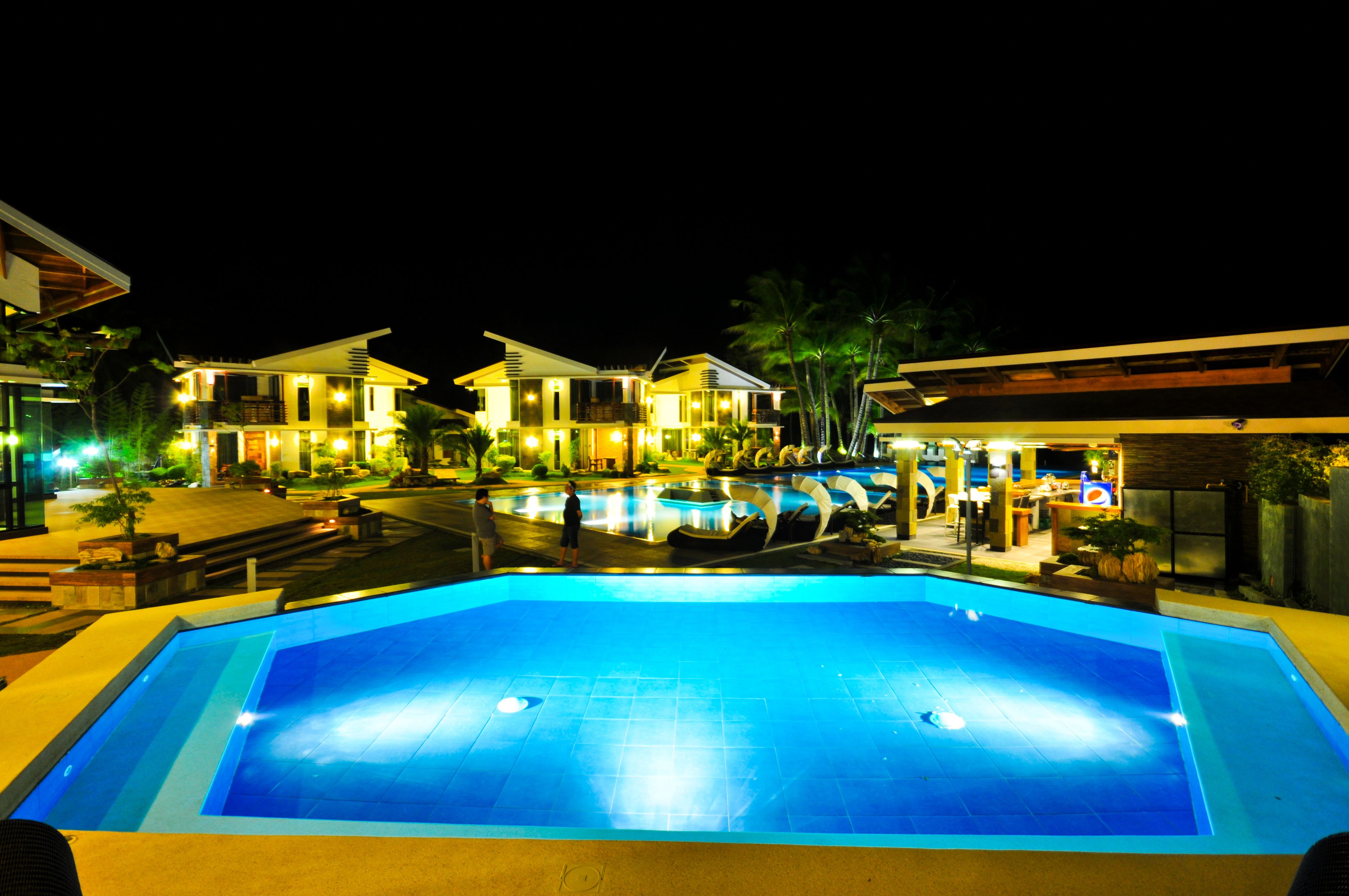 Vista noturna de um hotel com piscina, vários edifícios e iluminação externa.