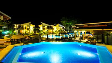 Vista noturna de um hotel com piscina, vários edifícios e iluminação externa.