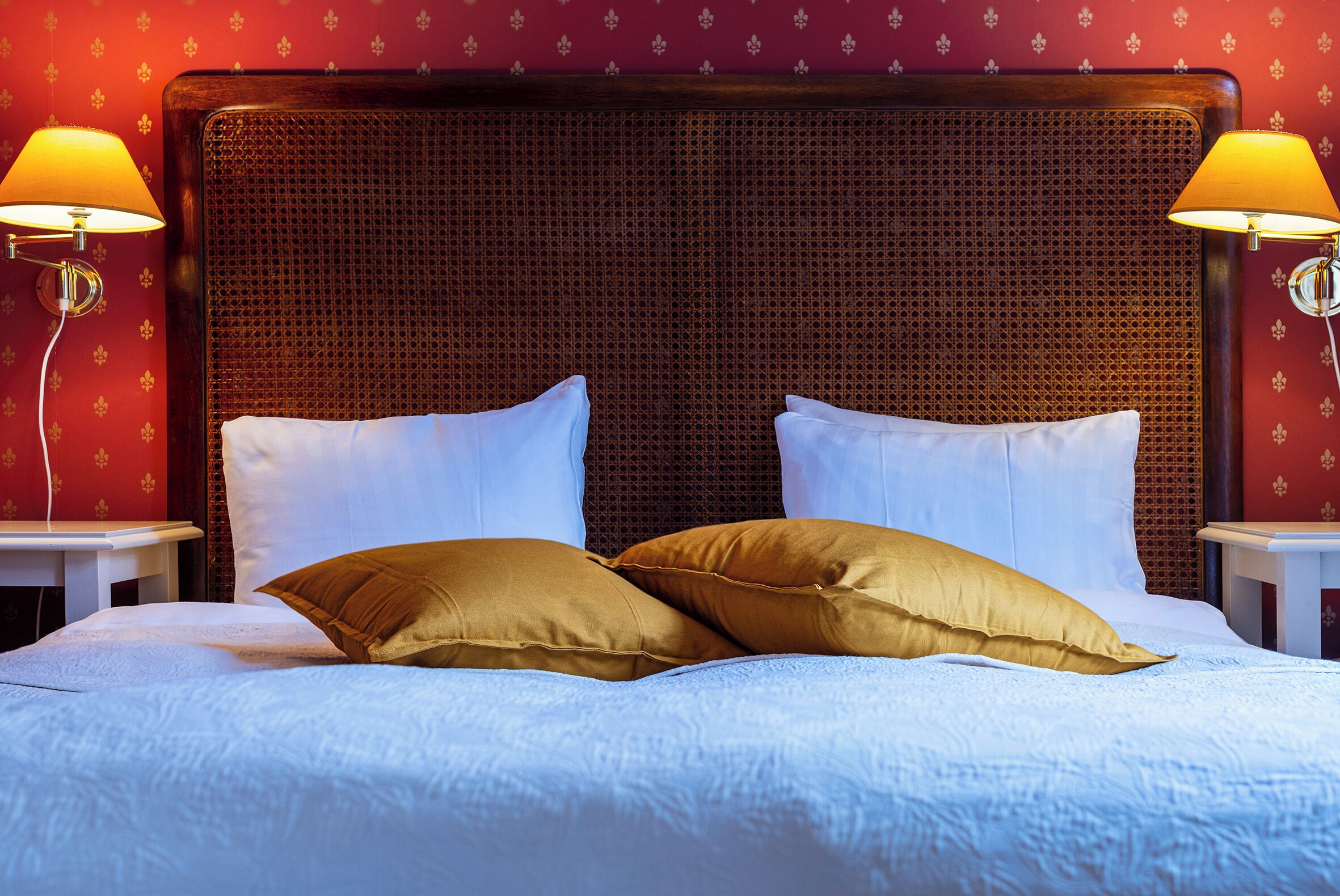 Cama com almofadas brancas e douradas, cabeceira de madeira e duas luminárias de cabeceira.