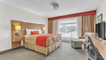 Quarto de hotel com cama, mesas de cabeceira, escrivaninha com cadeira, televisão e janela com cortinas.