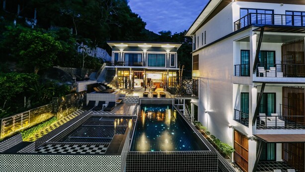 Um edifício moderno de vários andares com piscina, área de estar externa e entrada bem iluminada.