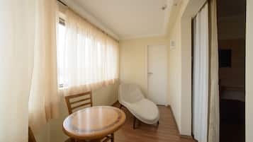 Um quarto com piso de madeira, uma mesa redonda com cadeiras, uma poltrona branca e uma porta.