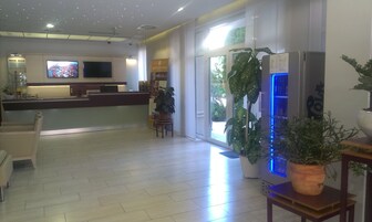 Um saguão de hotel com balcão de recepção, TV de tela plana e plantas em vasos.
