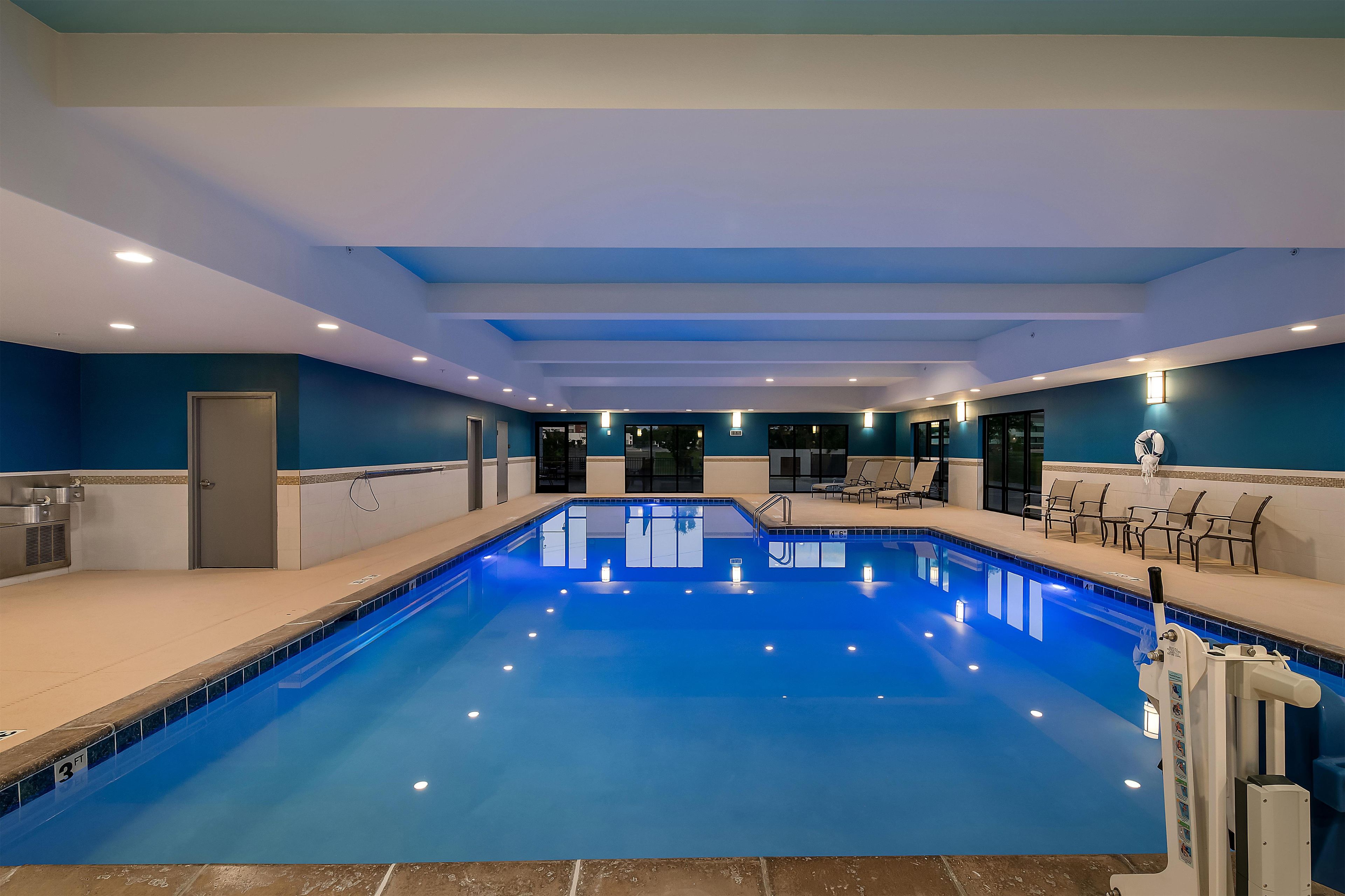 Piscina interna com superfície de água azul cristalina, rodeada por espreguiçadeiras e um deck revestido de azulejos.