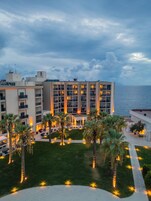 Um hotel com vários andares, área de estar externa e palmeiras.