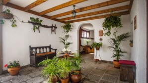 Interior rústico com vigas de madeira, soalho de pedra e diversos vasos de plantas.