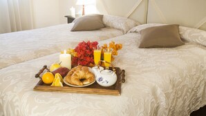 Cama bem arrumada com uma bandeja de itens de café da manhã, incluindo croissants, frutas e uma chaleira.