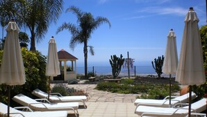 Uma área de estar à beira-mar com espreguiçadeiras e guarda-sóis, um gazebo e vista para o oceano.