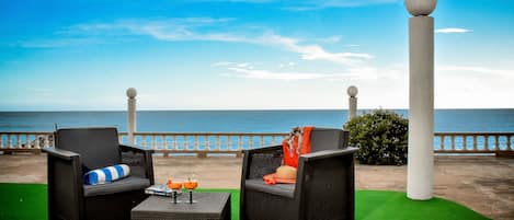 Um terraço com duas cadeiras de vime, uma mesa pequena com bebidas e vista para o mar.
