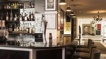 Uma área de bar com balcão polido, vários tipos de garrafas, copos e um quadro de cardápio.