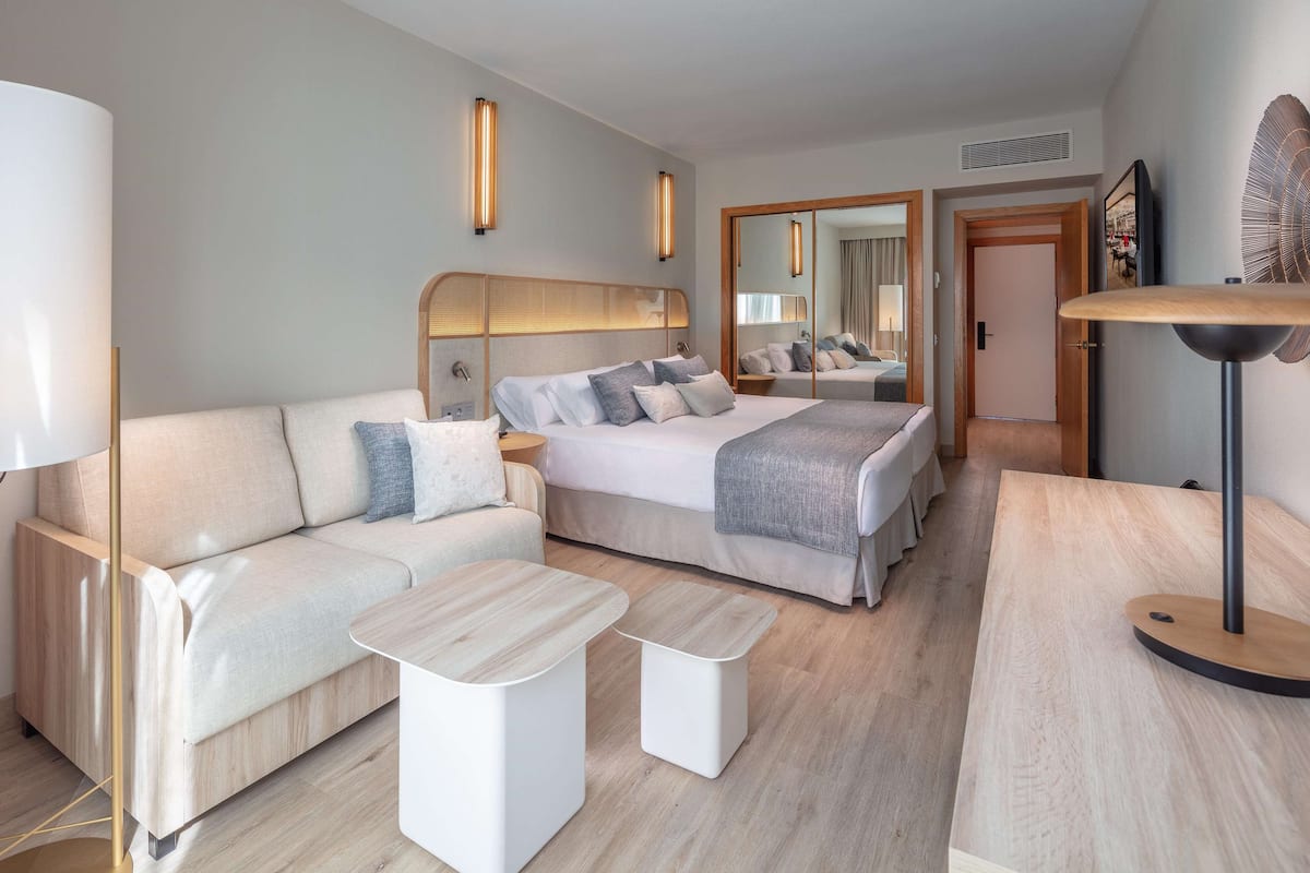 Quarto de hotel moderno com sofá, cama, mesa de cabeceira e abajur.