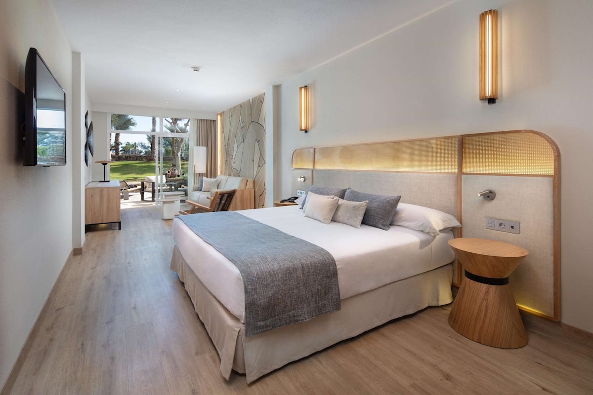 Quarto de hotel moderno com uma cama grande, uma mesa de cabeceira de madeira e uma TV fixada na parede.